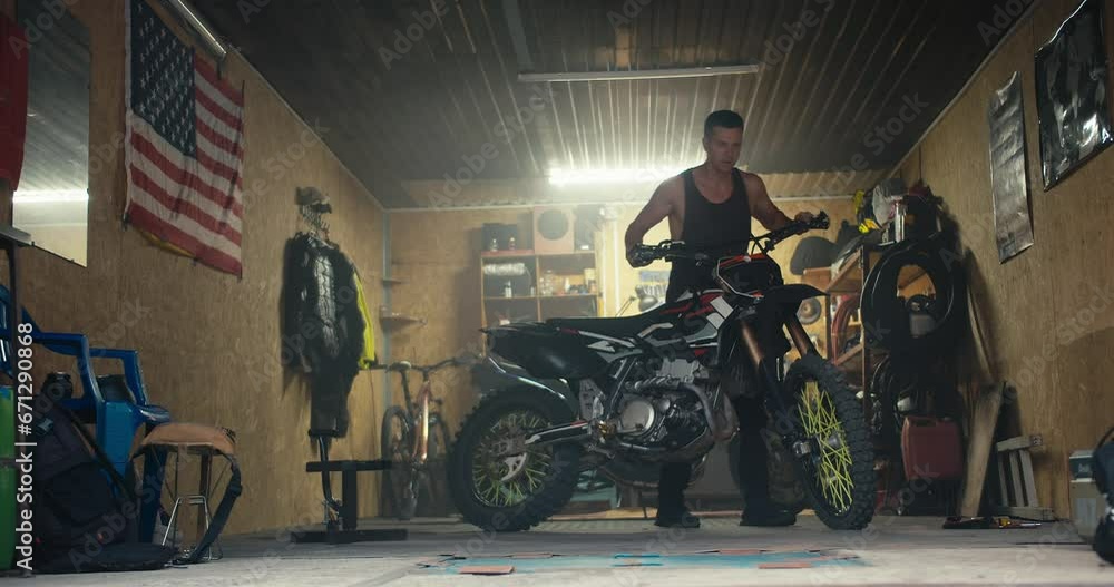 A male mechanic rolls out his motorcycle from his workshop garage with ...