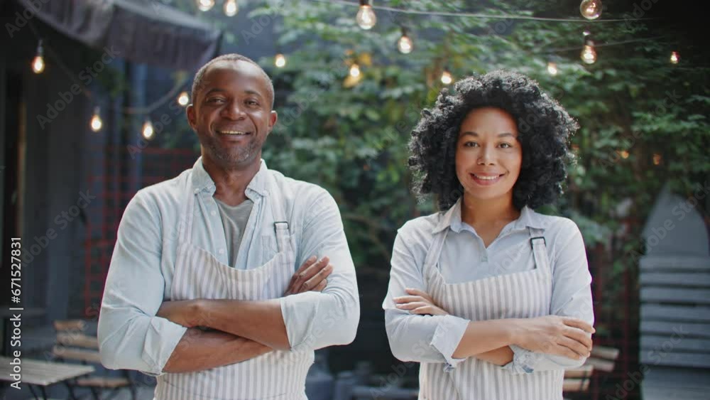 Two African American workers with aprons crossing hands while standing ...