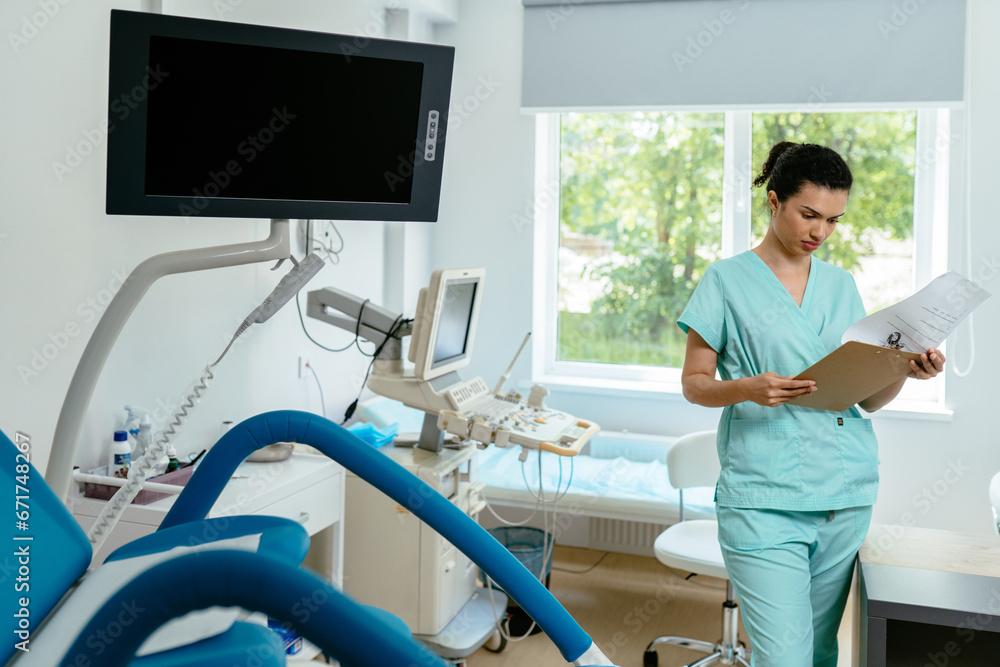 Portrait of gynecologist sitting near gynecological chair and ...