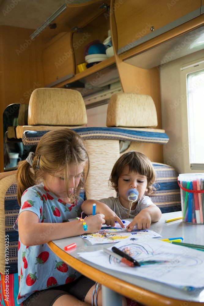 Two caucasian children, brother and sister, drawing on a campervan ...