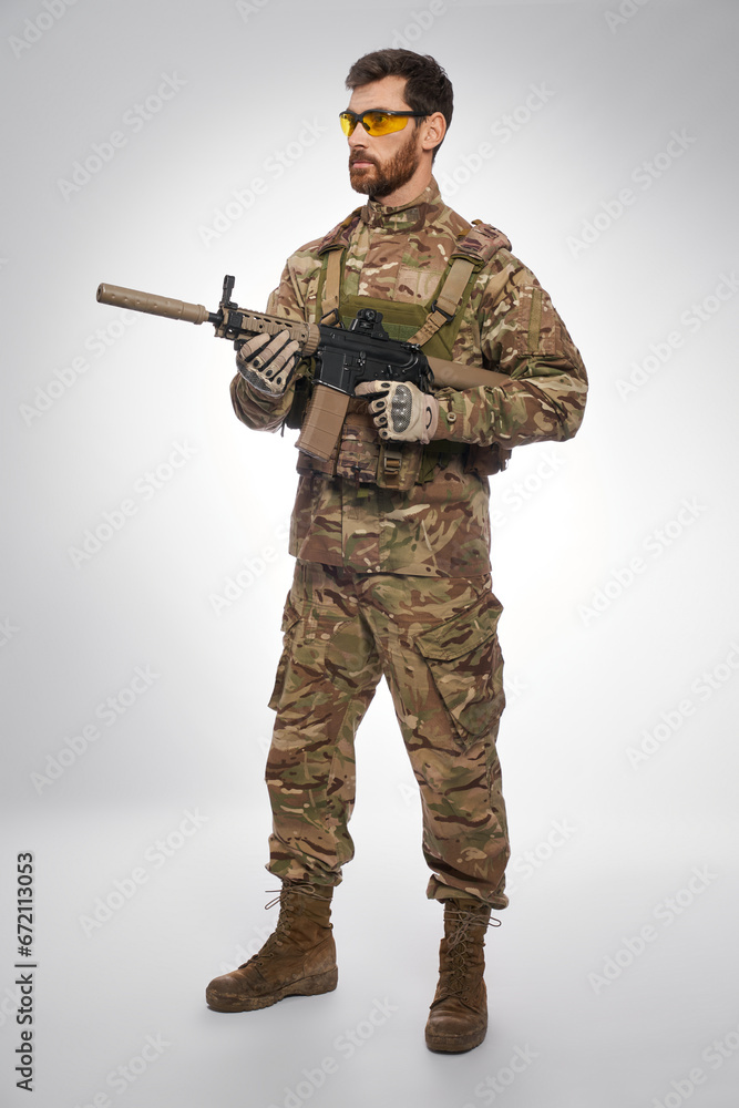 Focused dark-haired soldier in armor vest holding machine gun, looking ...