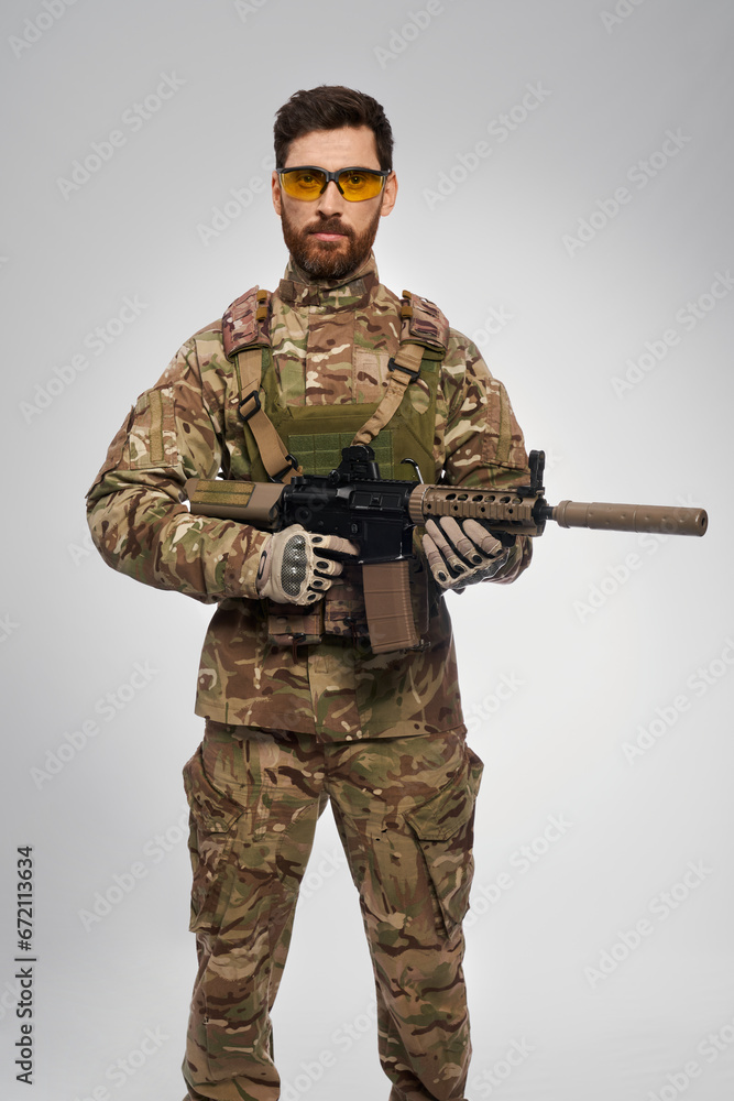 Armed military man posing with assault weapon in studio. Front view of middle-aged infantryman ...