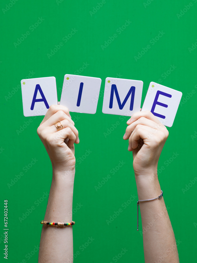 Mot AIME en carton et bois tenue par une main d'enfant sur fond vert ...