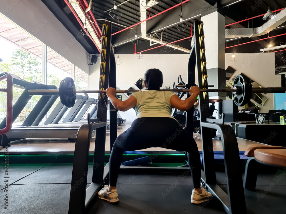back view of woman doing squat exercises. squat training with a barbell ...