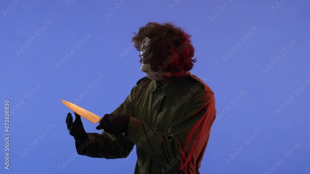 Man in white mask with big sharp knife on blue background with red neon ...