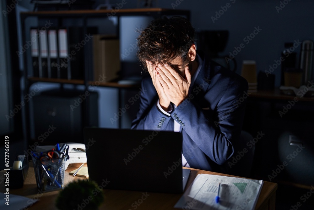 Hispanic young man working at the office at night with sad expression ...