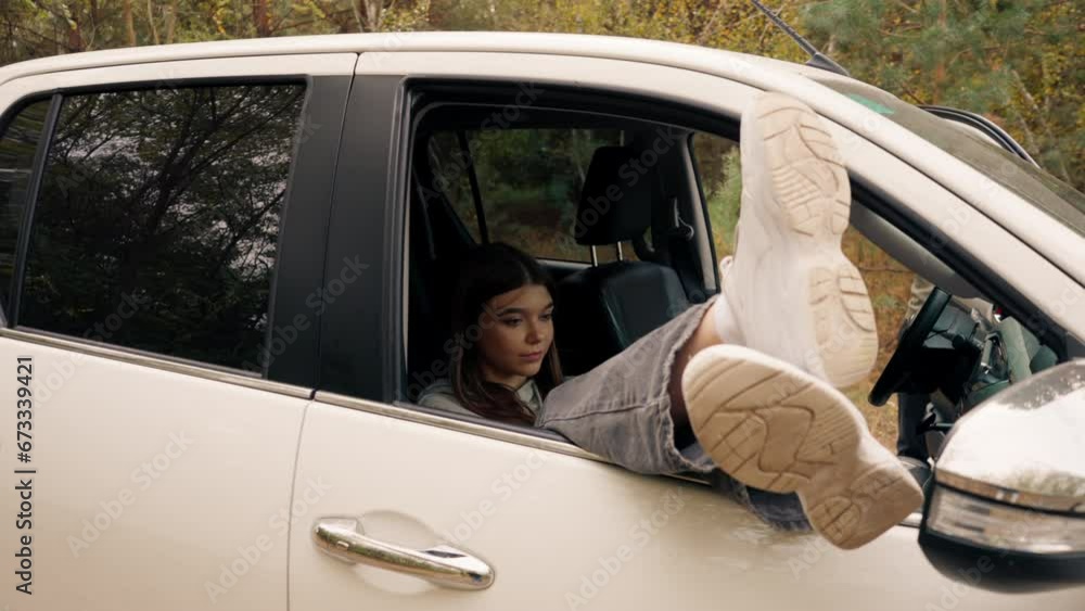 A girl sits in the car in the front passenger seat stretching her legs ...