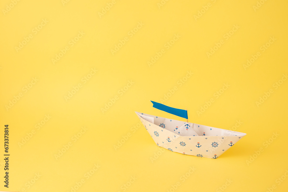Paper boat on a yellow background, with anchor print. With a flag where ...