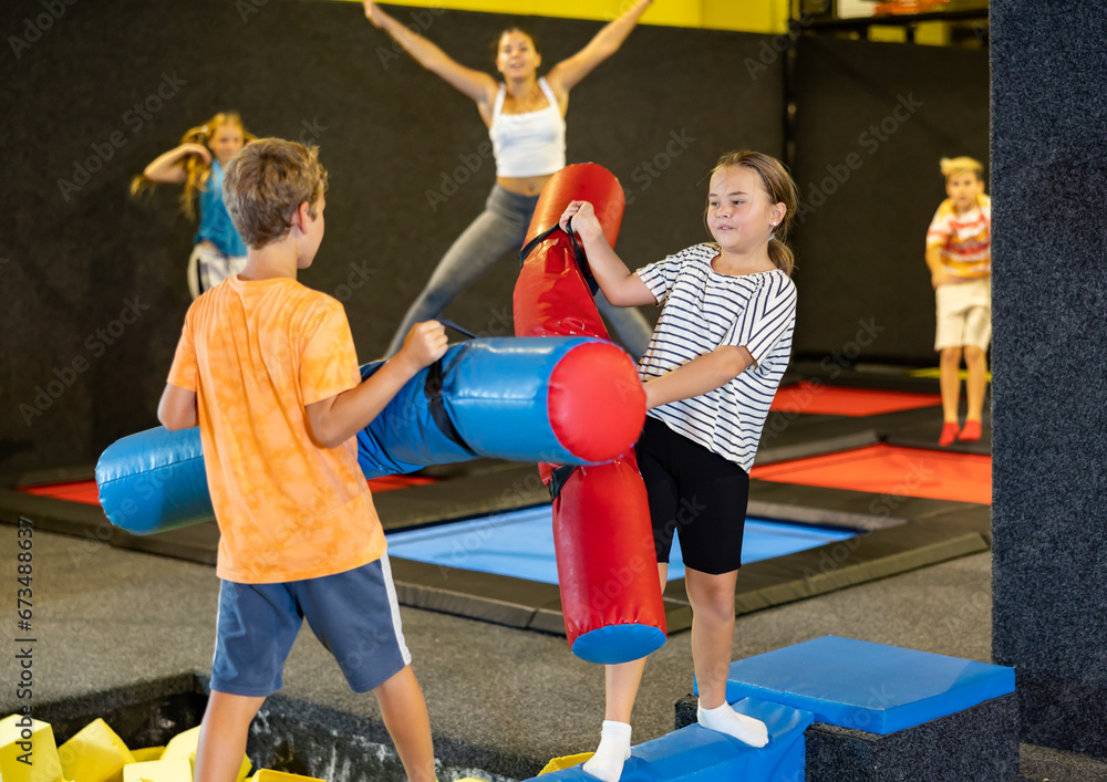Expressive determined tween girl having funny wrestling by pugil sticks ...