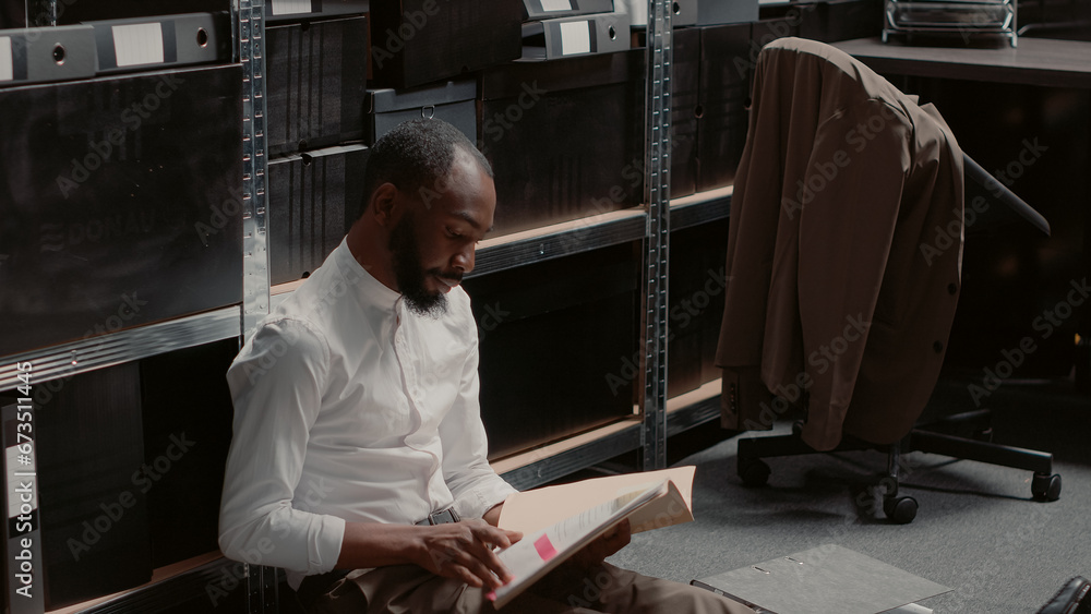 Police officer sitting on archive room floor with files conducting ...