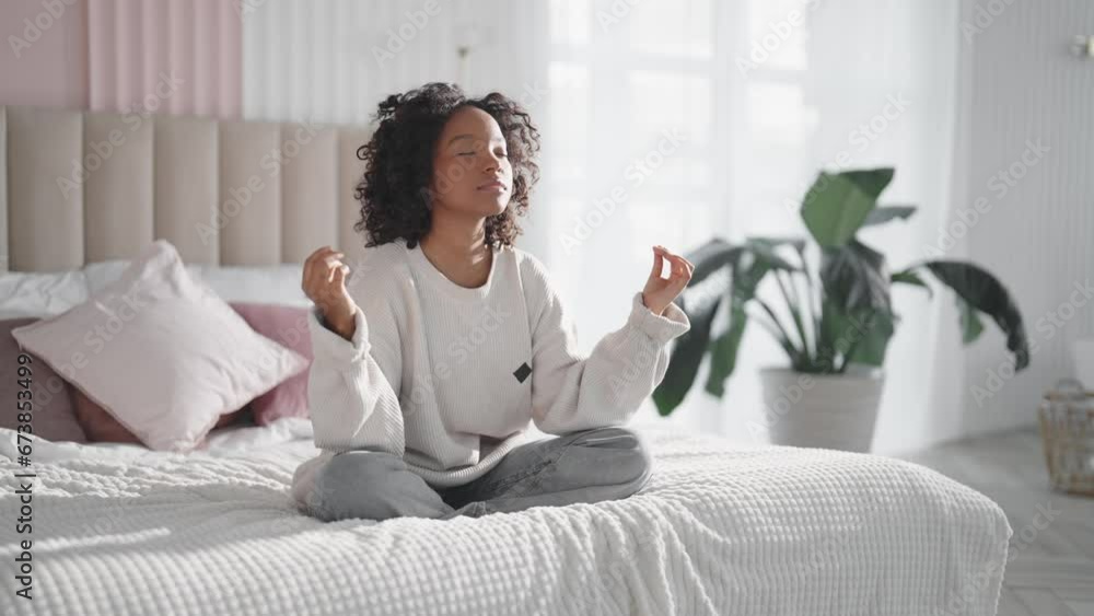 Smiling African american curly woman meditating sitting in bed at home ...