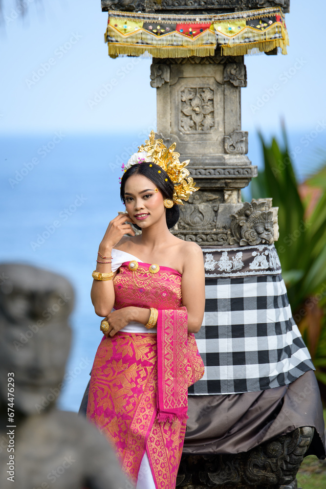 Young woman in traditional Balinese attire stands before an ancient ...