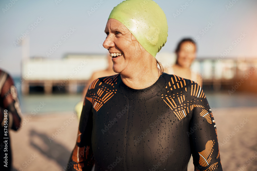 Mature woman in a wetsuit laughing on a beach with her swimming group ...
