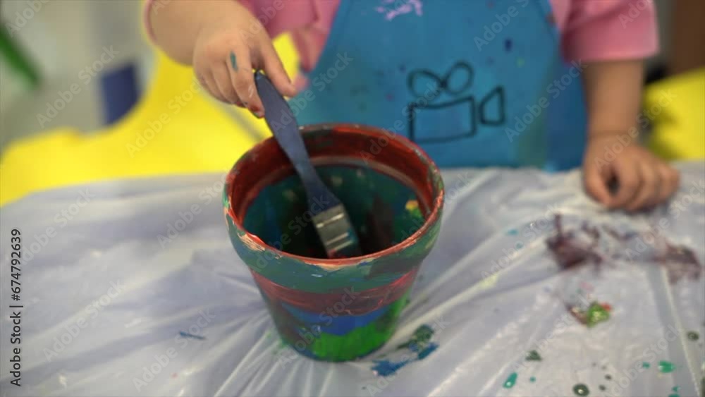 Little kid, a toddler age, colouring a pot with messy colours and ...