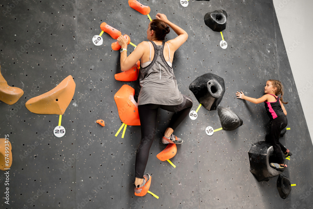 Mother and daughter climbing wall in gym. Adult woman and her child ...