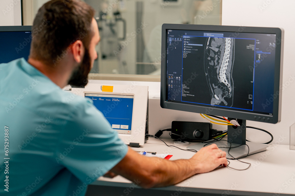 A radiologist sits at a table behind a computer monitor and examines a ...