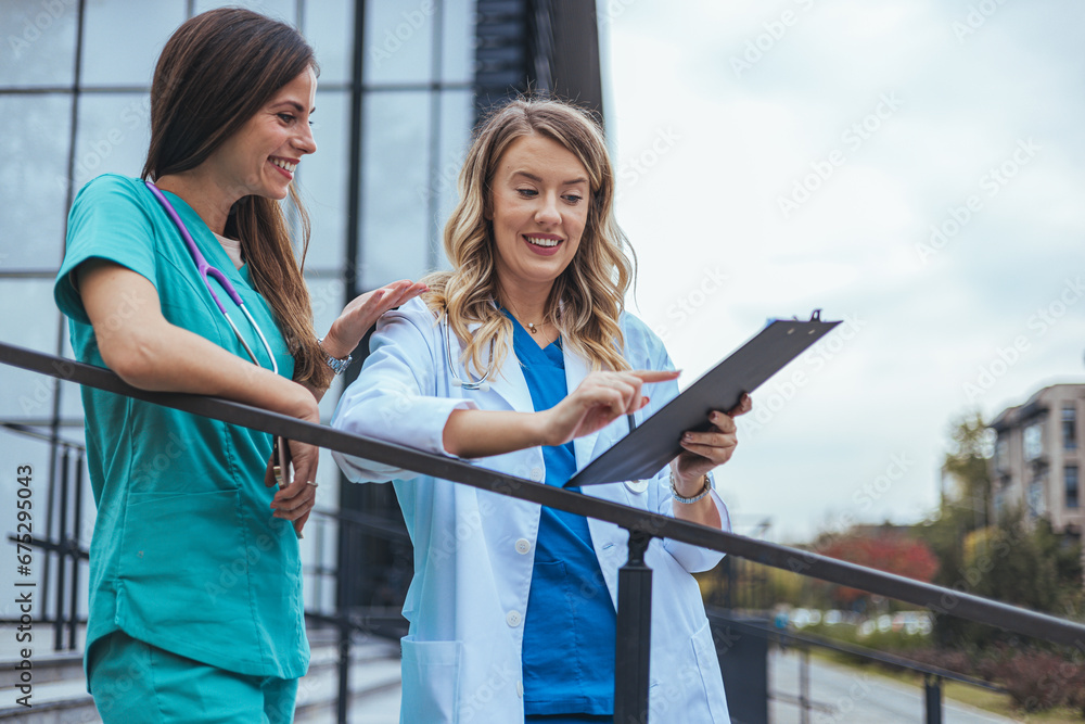 Two female doctor walk down an elevated walkway together. One wears a ...