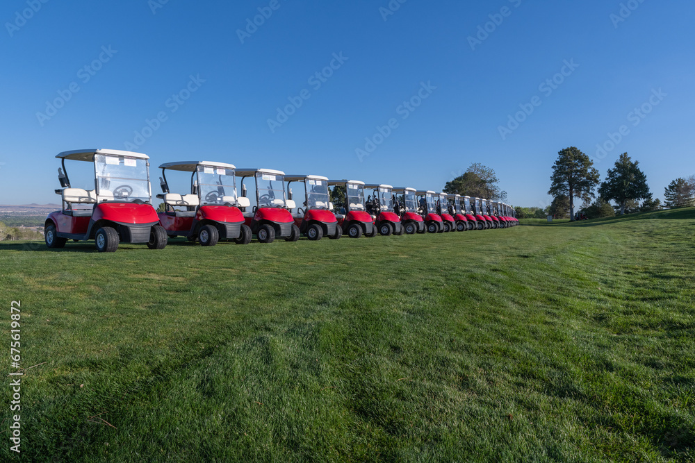 Golf carts parked in a row on the driving range of a golf course with a ...