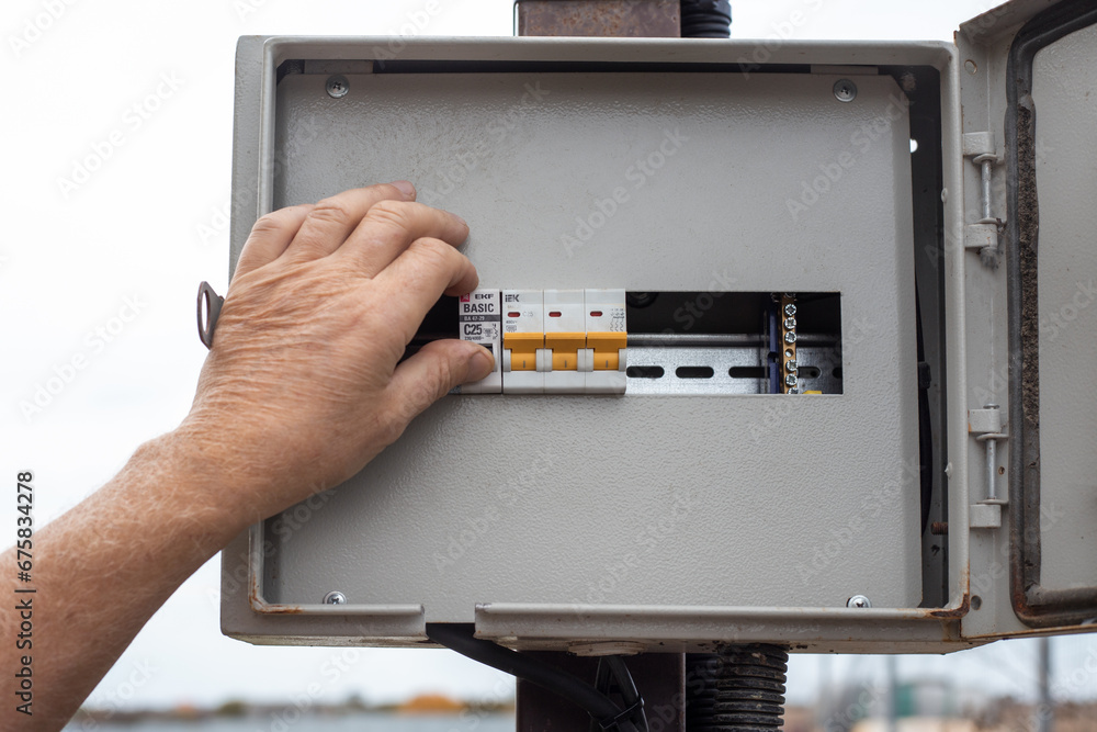 A man switches the toggle switches of the electrical panel on the pole ...
