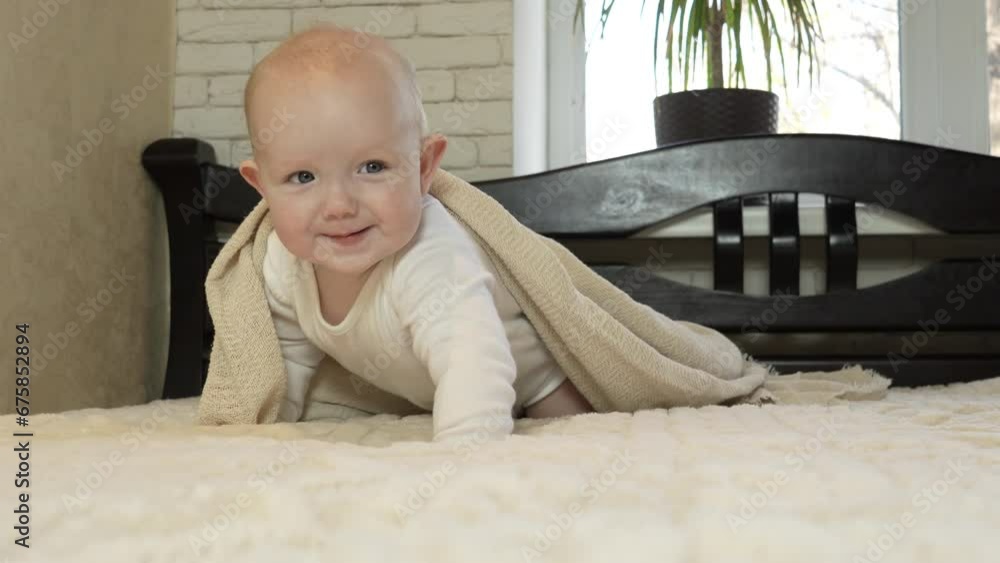 A playful little boy stands on all fours on the bed and smiles ...
