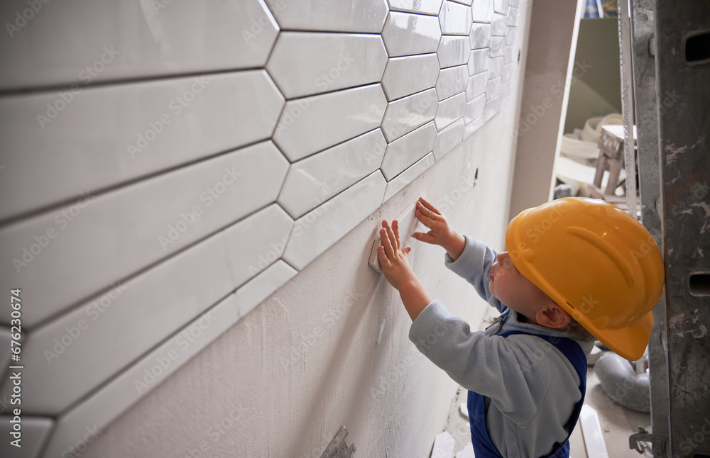 Little child construction worker installing ceramic tile on the wall in ...
