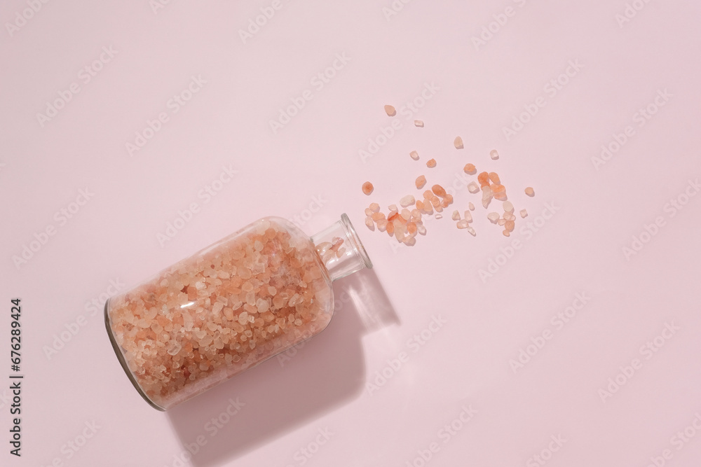 Pink salt grains are poured into a pastel pink background from a ...