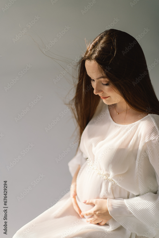 Cute young Pregnant girl sitting on the white studio in warm light with ...