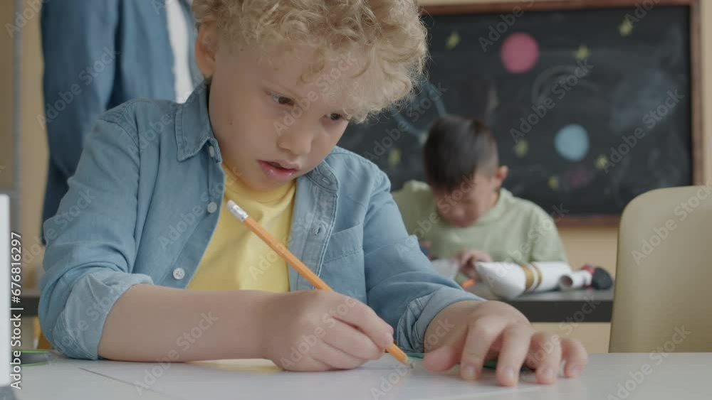 Little kid with blond curly hair putting marks on paper sheet with ...