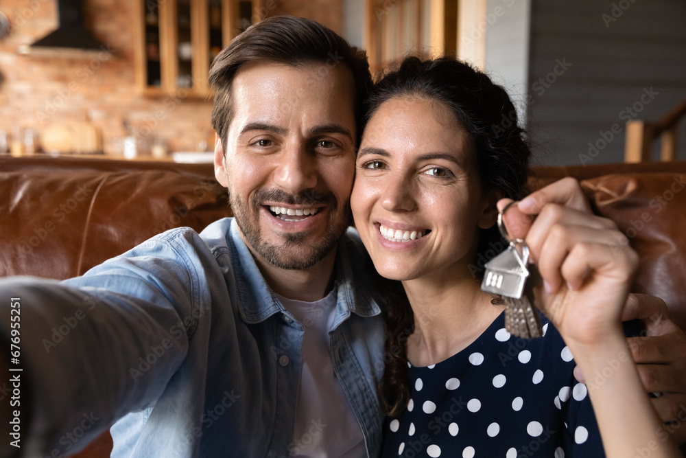 Head shot happy young couple showing keys, hugging, sitting on couch ...
