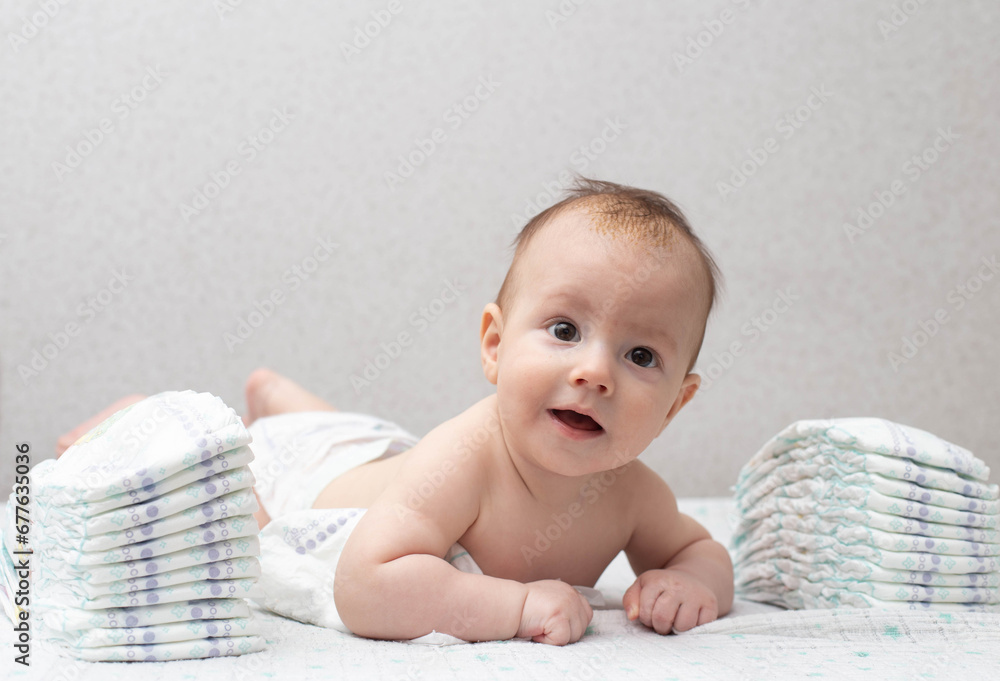 A little boy at the age of 5 months lies in a diaper on a white ...