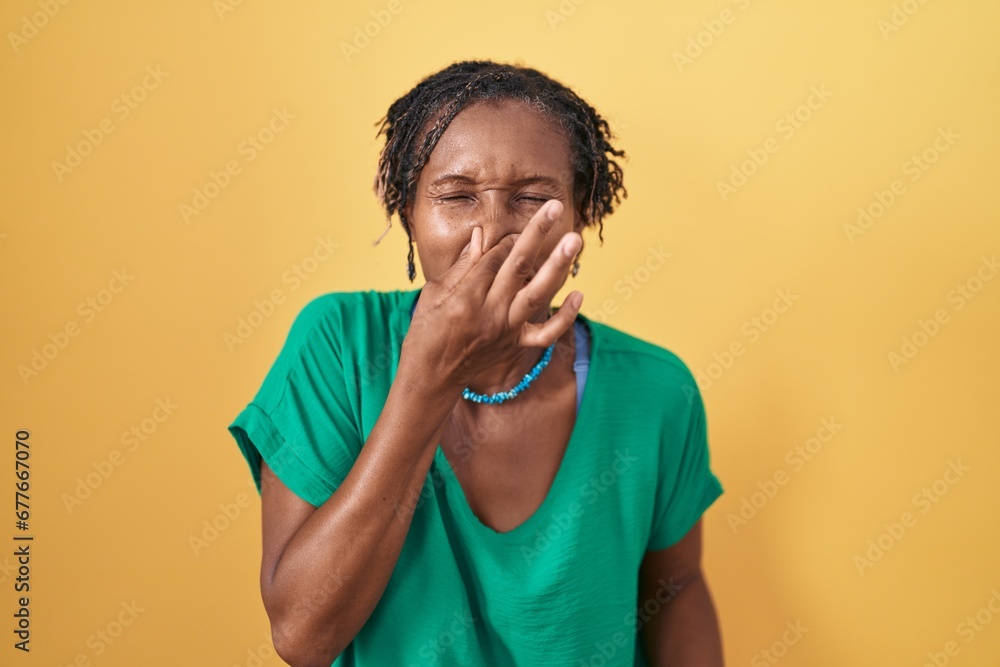 African woman with dreadlocks standing over yellow background smelling ...