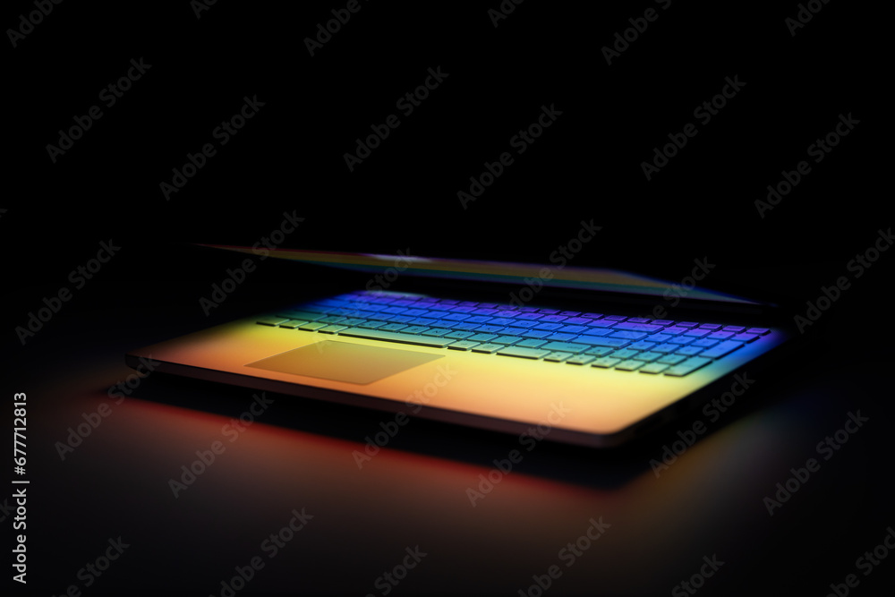 half closed laptop on dark table with colourful light reflection on ...