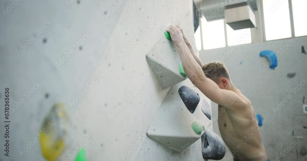 Fit young man using hand and footholds to climb up an artificial wall ...