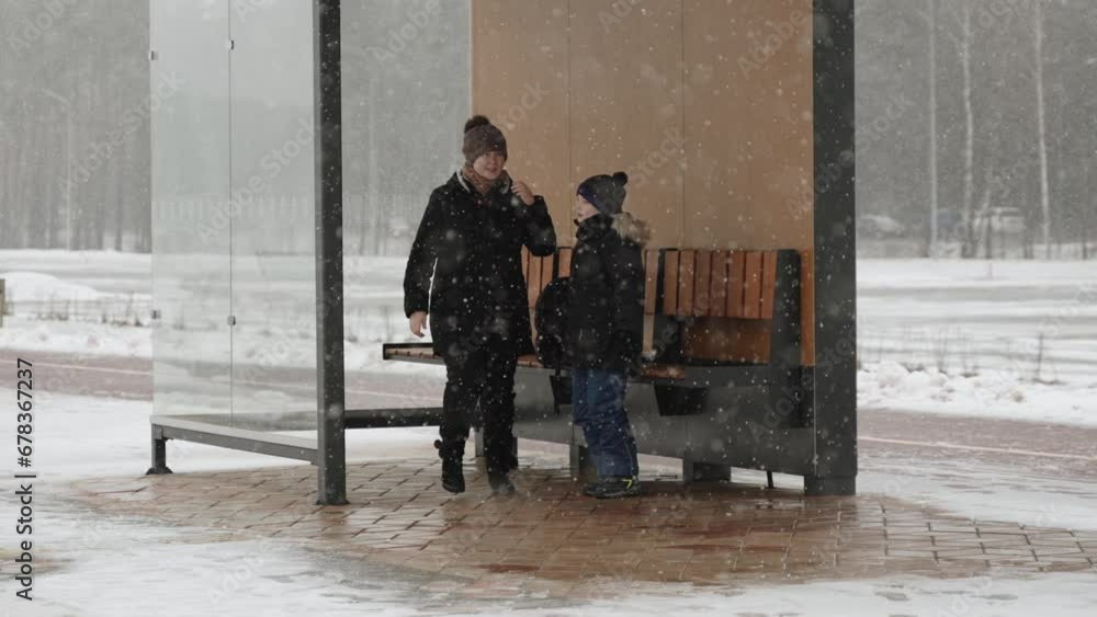 Mother and son warm up at public transport stop on frosty winter day ...