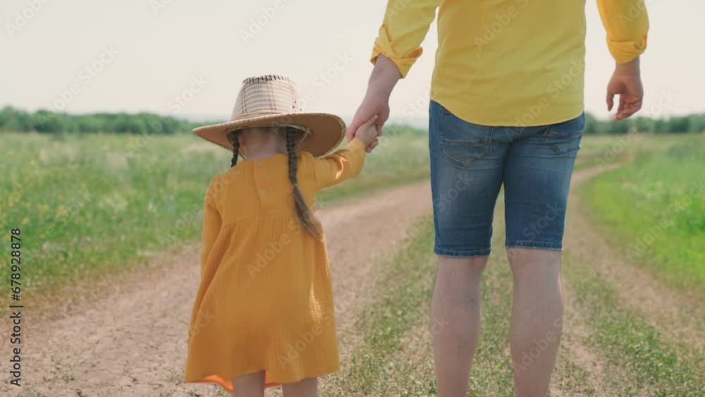 Little daughter, dad are walking holding hands in field. Child, dad go ...