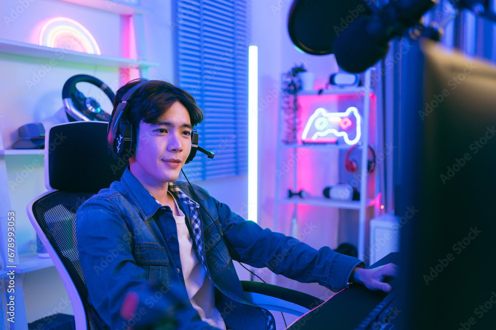 A young Asian man professional gamer wearing jeans jacket sits on a ...