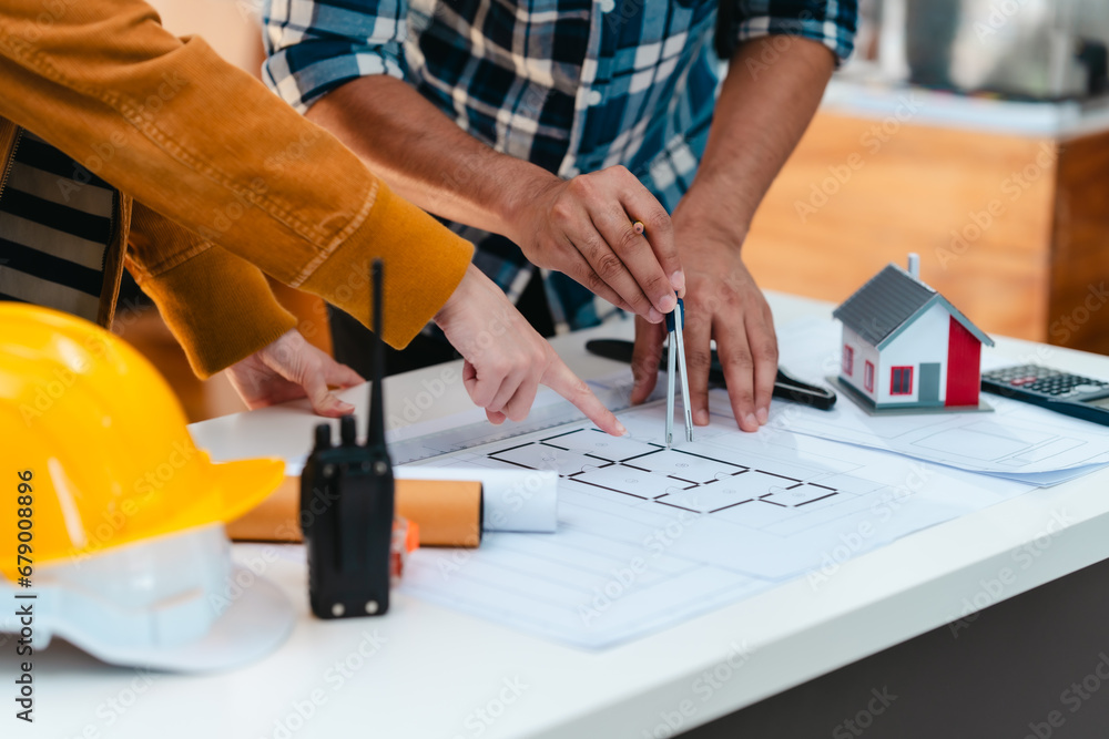 two people working on architectural plans with a model house, safety ...