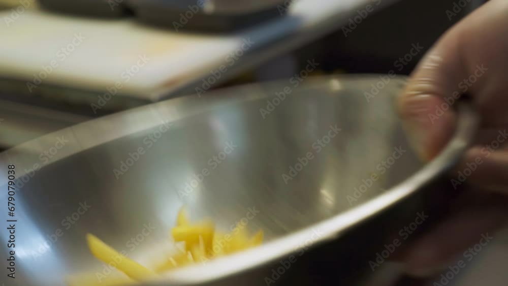 A cook is mixing the french fries in the dish inside of the restaurant ...