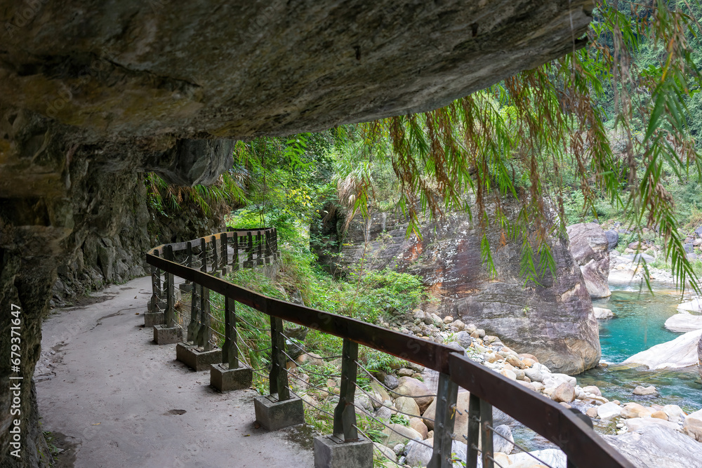 A secluded walking trail under an overhanging rock cliff offers a view ...