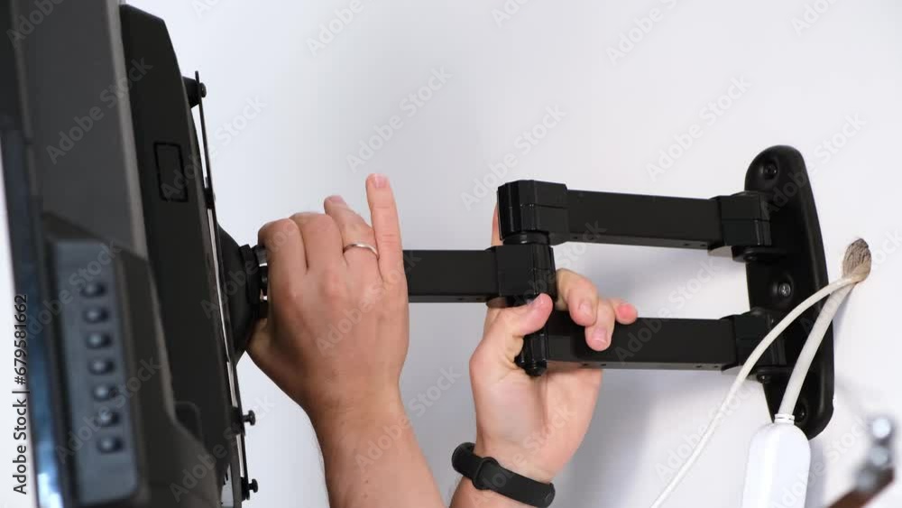A man rotates a flat-screen TV hanging on a bracket, demonstrating a ...
