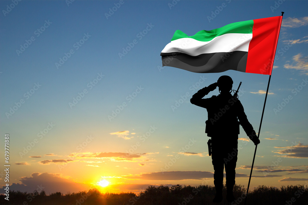 Silhouette of saluting soldier with the flag of UAE against the sunset ...