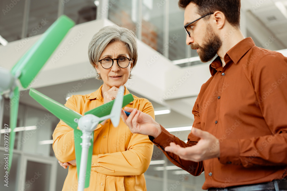 Senior woman and middle aged man using windmill working in modern office. Team serious engineers ...