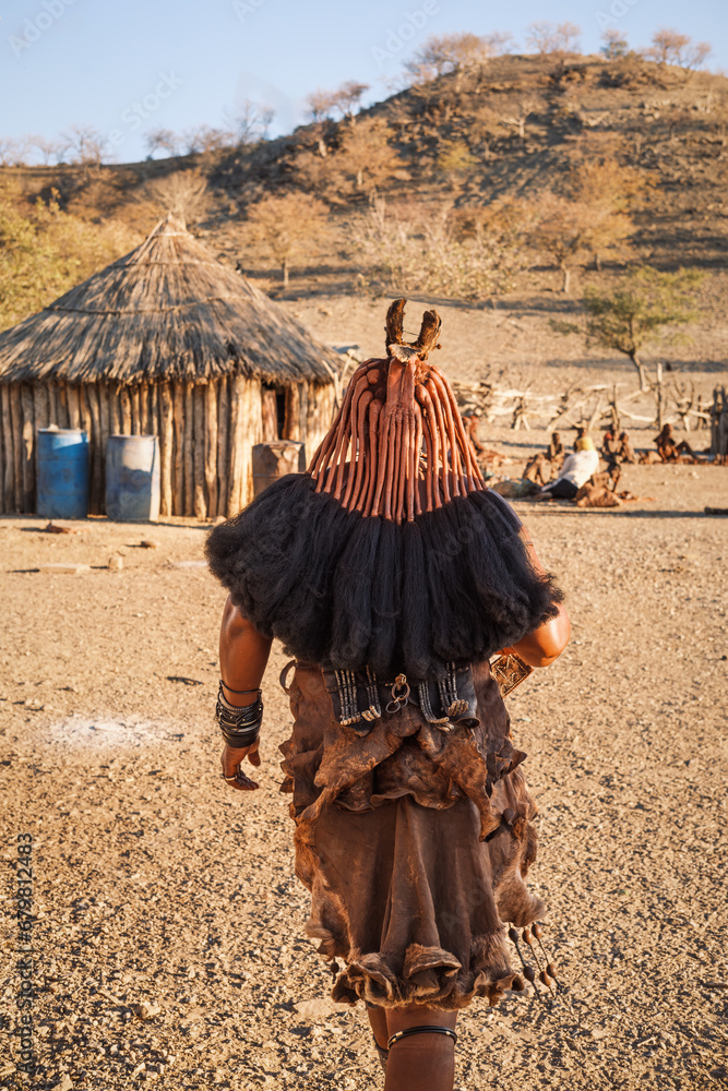 Himba woman in traditional attire walking towards her hut in a small ...