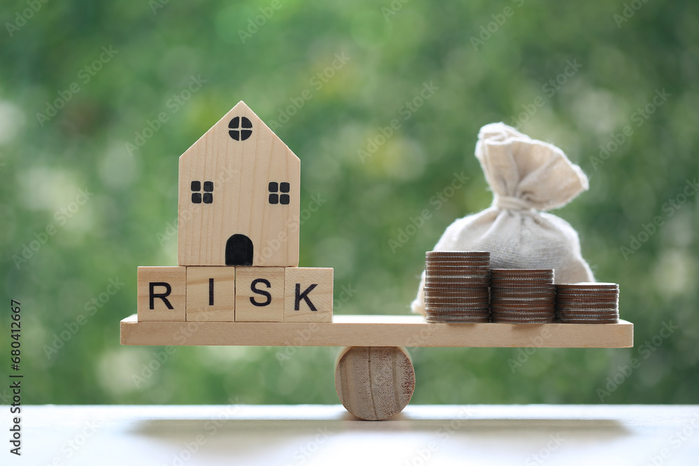 Model house with wording risk and money bag on wood scale seesaw on ...