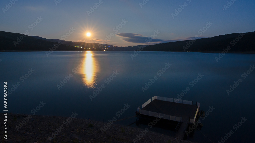 Under the glow of a full moon, a serene lake unveils its calm waters. A ...