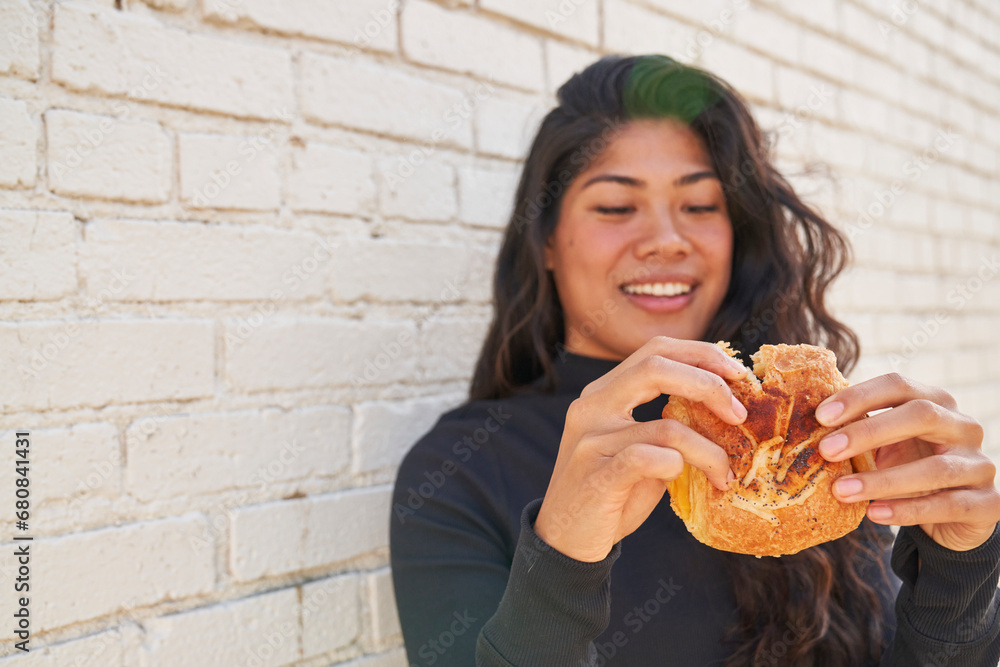 Woman eating savory pastry outdoors in front of white brick wall ...