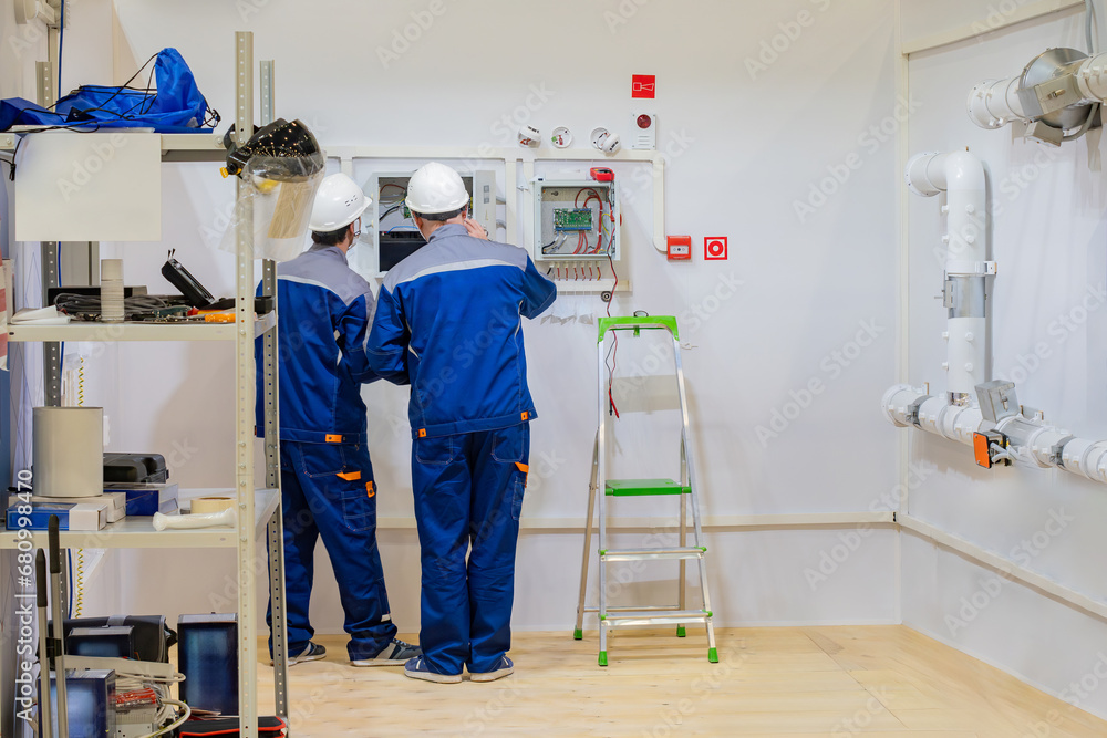 Two man electricians with backs to camera. Power cabinet repair ...