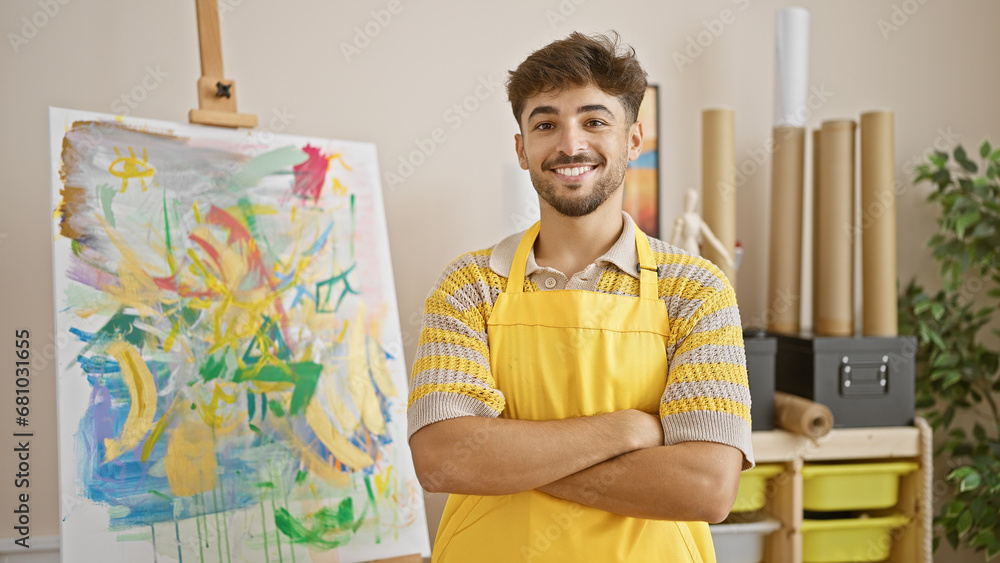 Confident young arab man, arms crossed, smiling at canvas in art studio ...