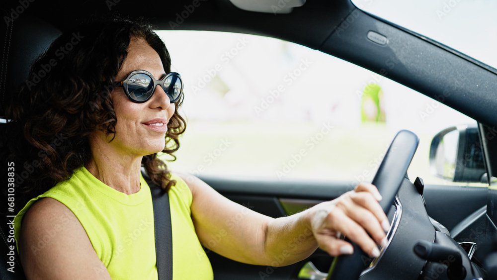 Middle age hispanic woman driving a car smiling wearing sunglasses on ...