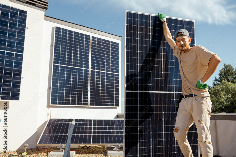 Portrait of a man standing with solar panel on a rooftop of his house ...